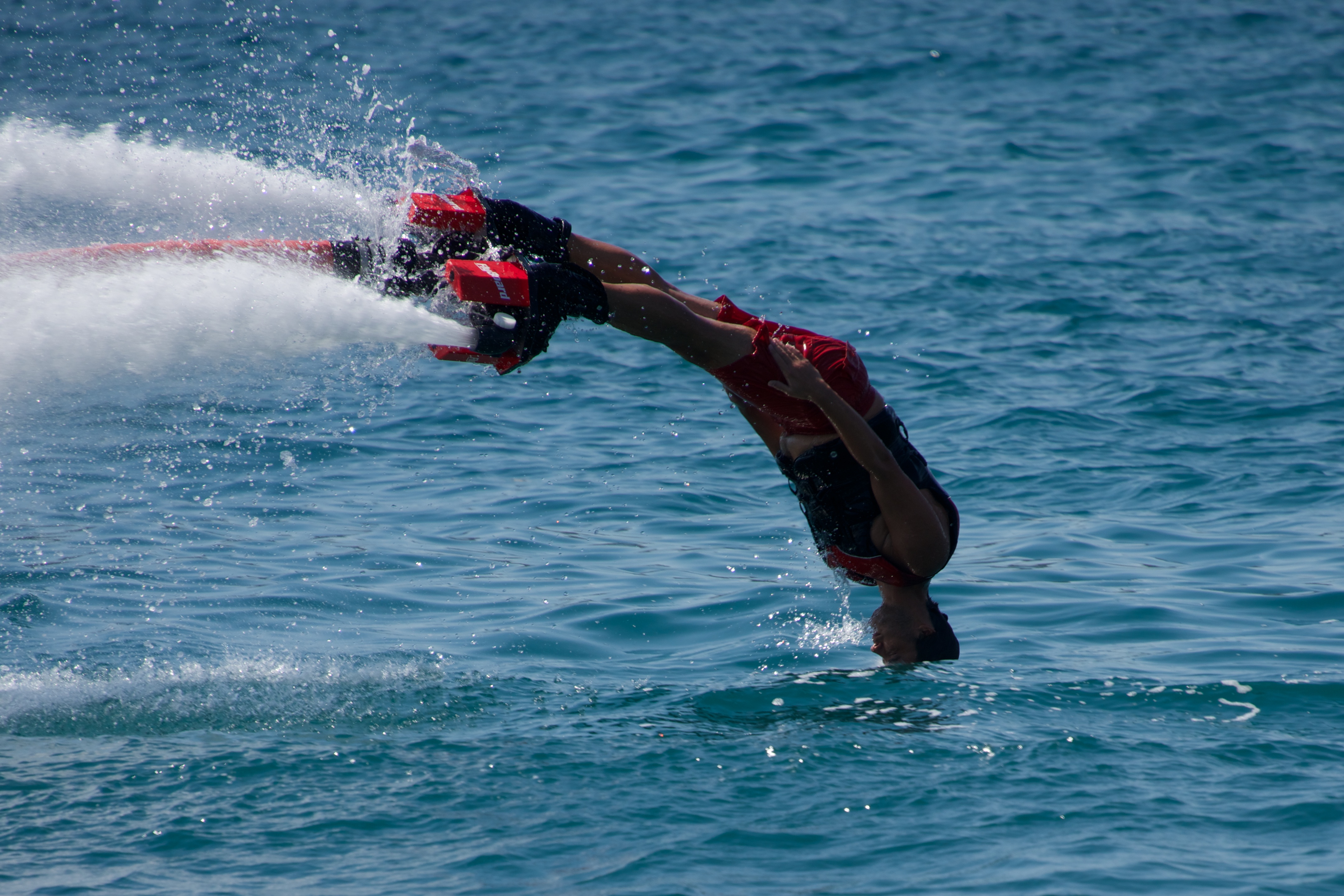 Flyboarder in red diving headfirst into sea - Nick Dale - Private Tutor