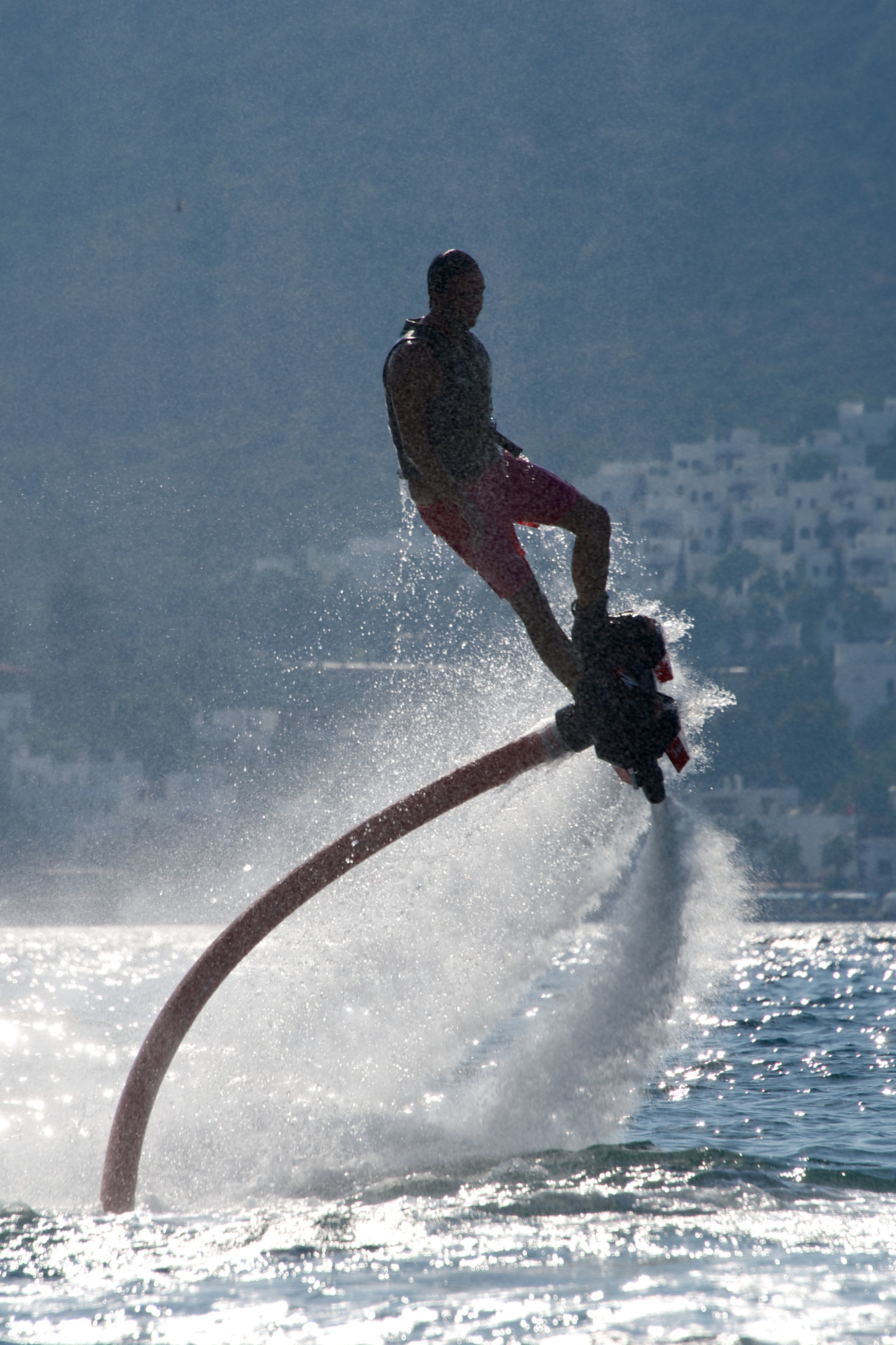 Flyboarder in silhouette spiralling over backlit waves | Nick Dale ...